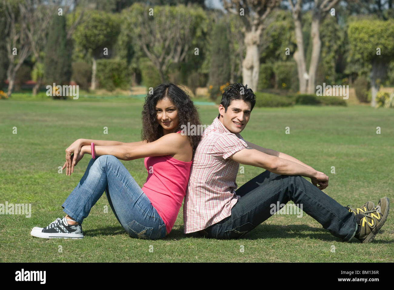 Couple sitting back to back in a park Stock Photo - Alamy