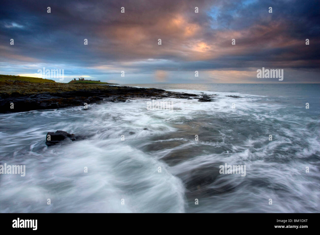 View along coastline on a stormy day towards the ruins of Dunstanburgh ...