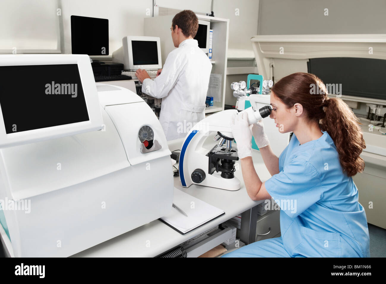 Female lab technician analyzing a sample through a microscope Stock ...