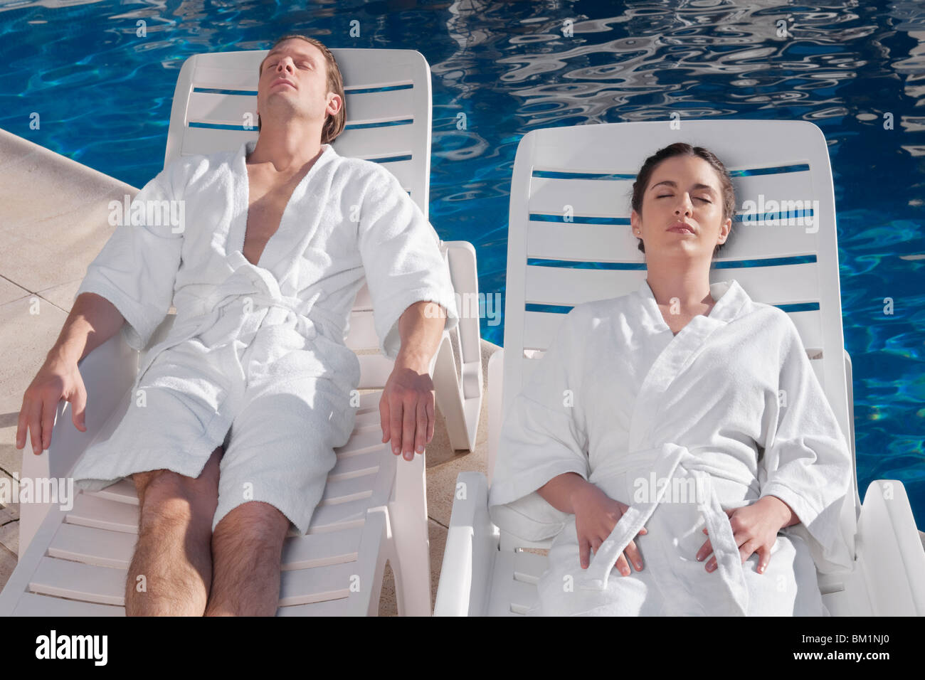 Couple resting on lounge chairs at the poolside Stock Photo - Alamy