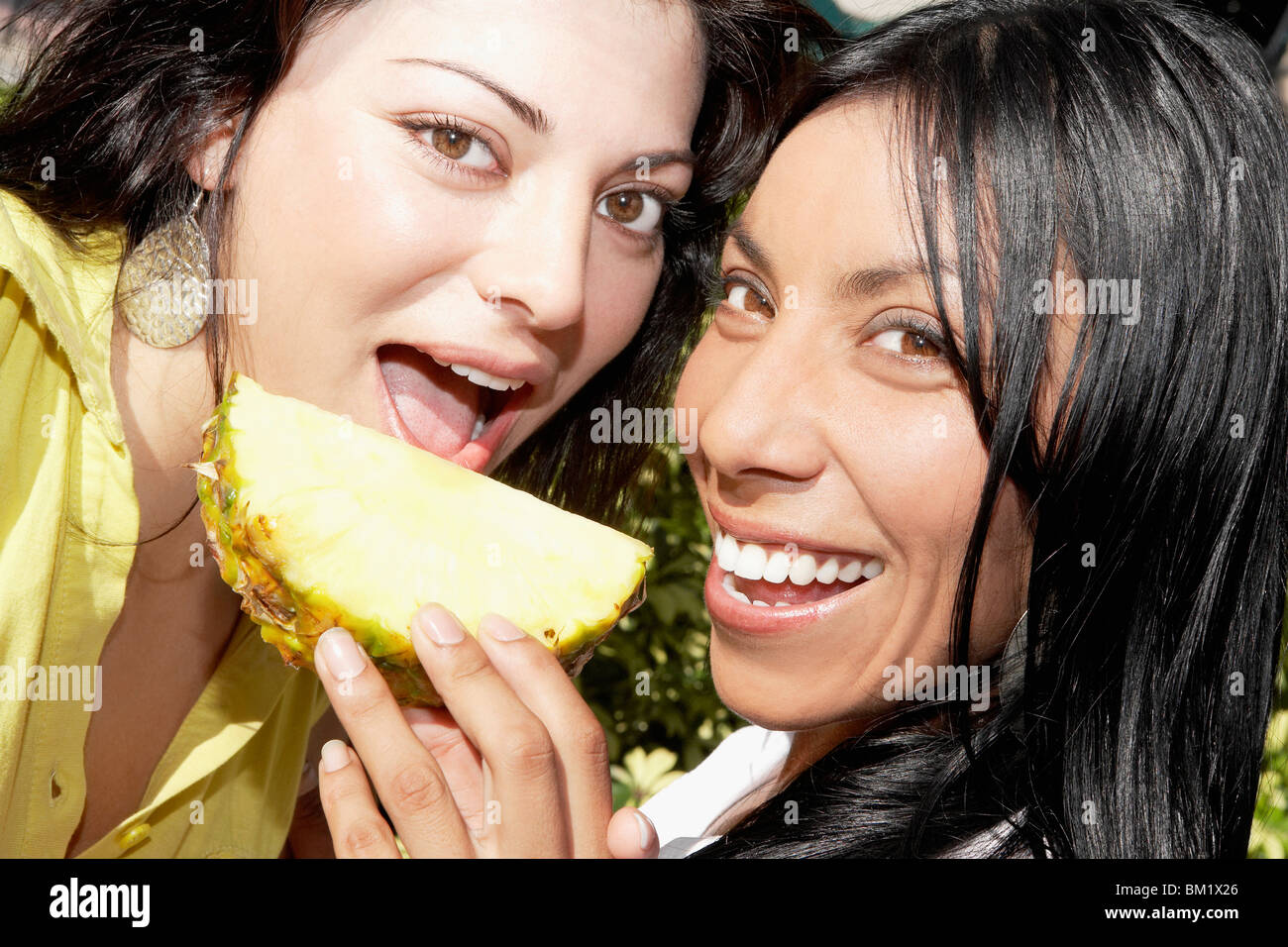 Portrait of two women eating a slice of pineapple Stock Photo - Alamy