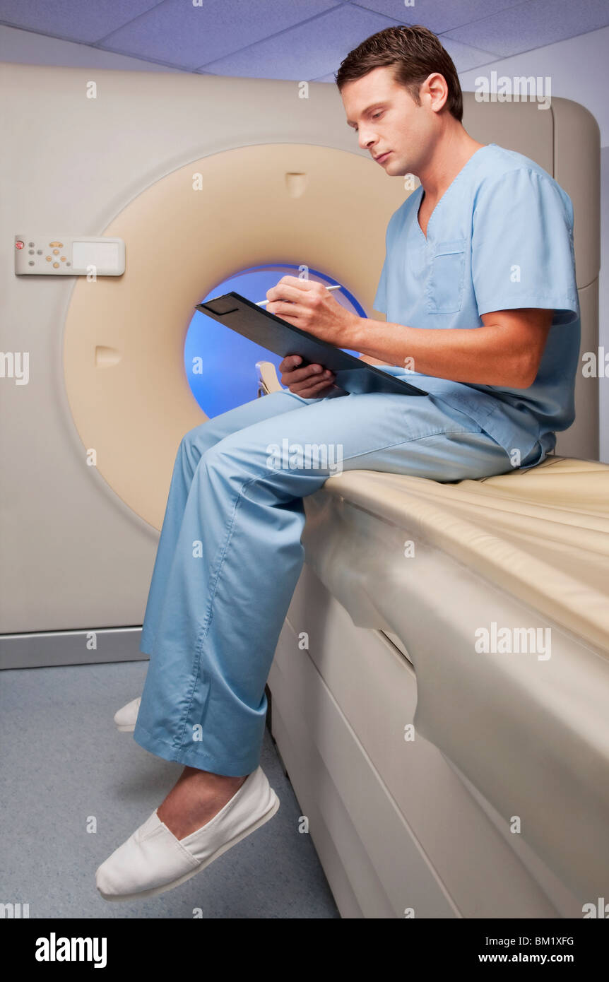 Healthcare worker sitting on a CAT scan machine and writing on a ...