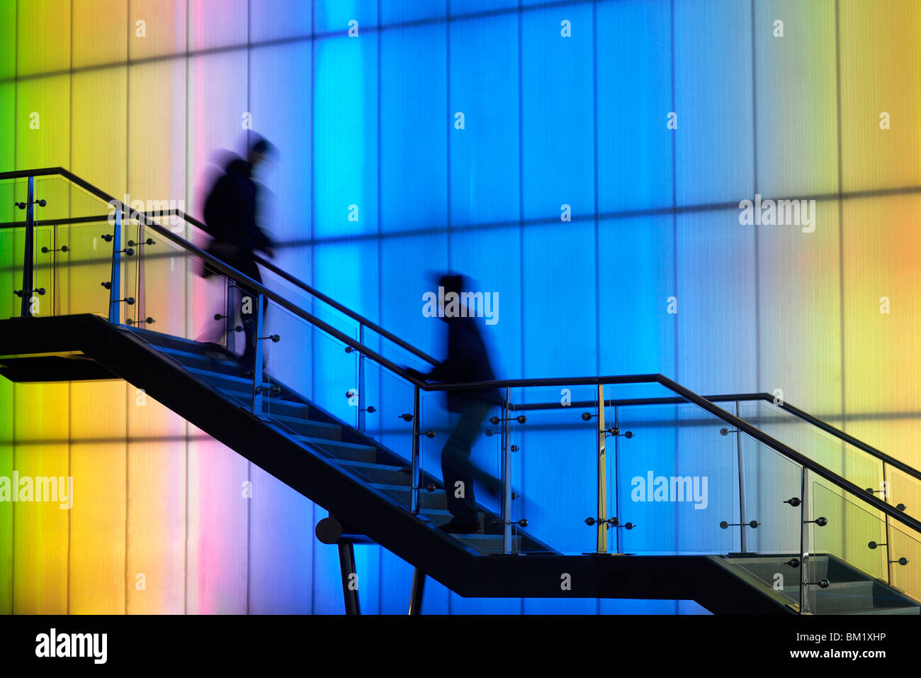 two people passing on stairs in front of a coloured light wall Stock ...