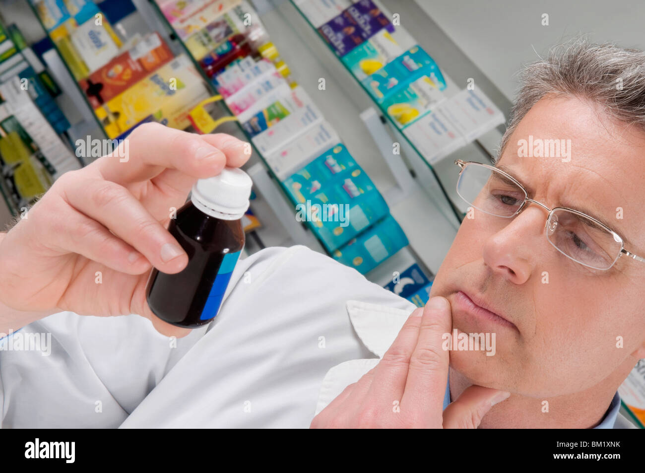Pharmacist holding a medicine bottle and thinking Stock Photo - Alamy