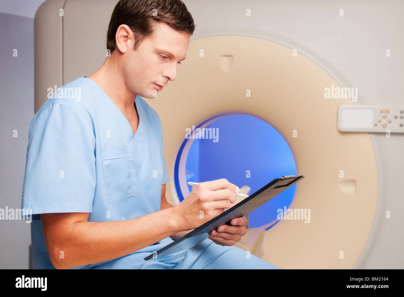 Healthcare worker sitting on a CAT scan machine and writing on a ...