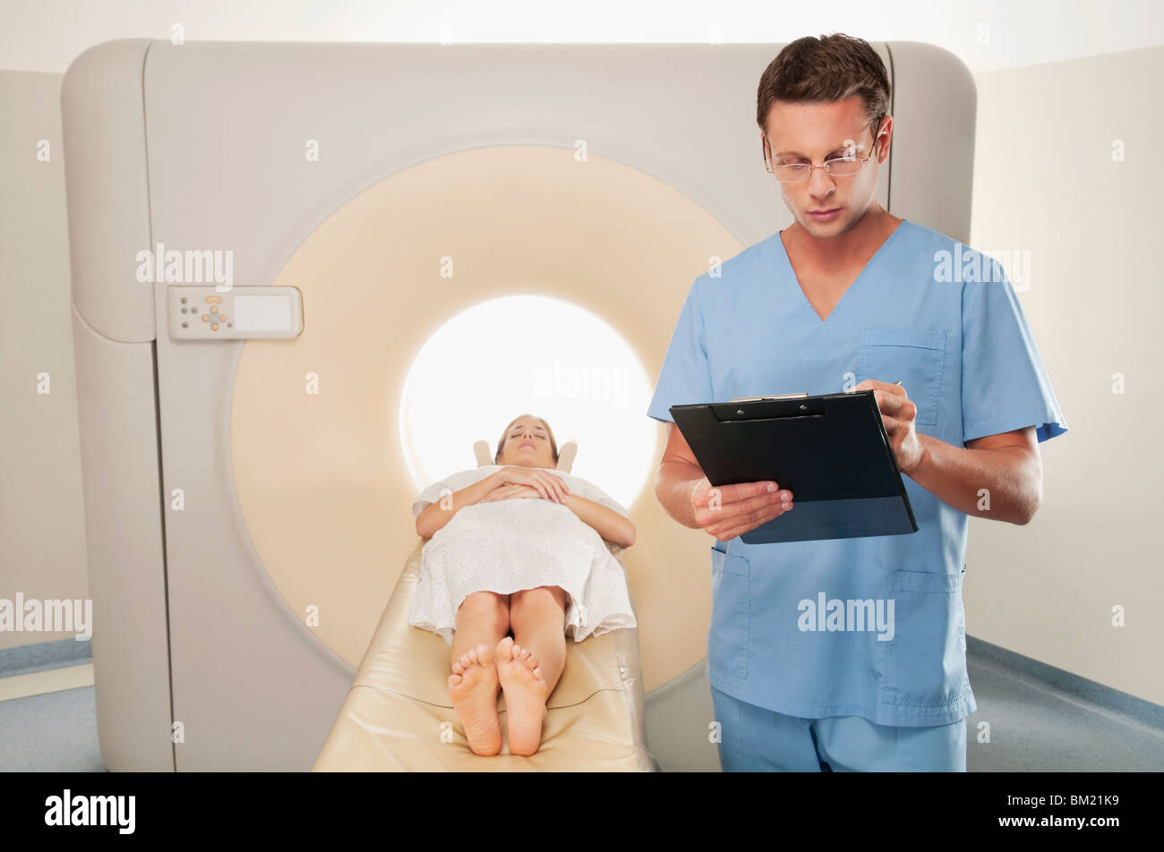 Surgeon checking medical report with a patient undergoing an MRI scan ...