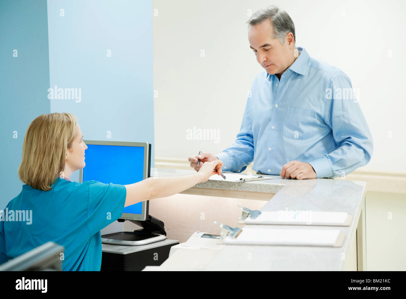 Female nurse helping a patient in filling form at a reception counter ...