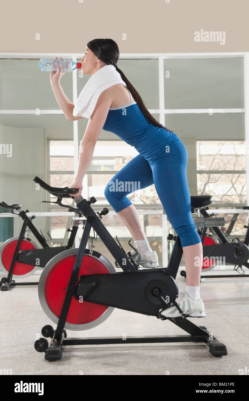 Woman drinking water and working out on an exercise bike Stock Photo ...