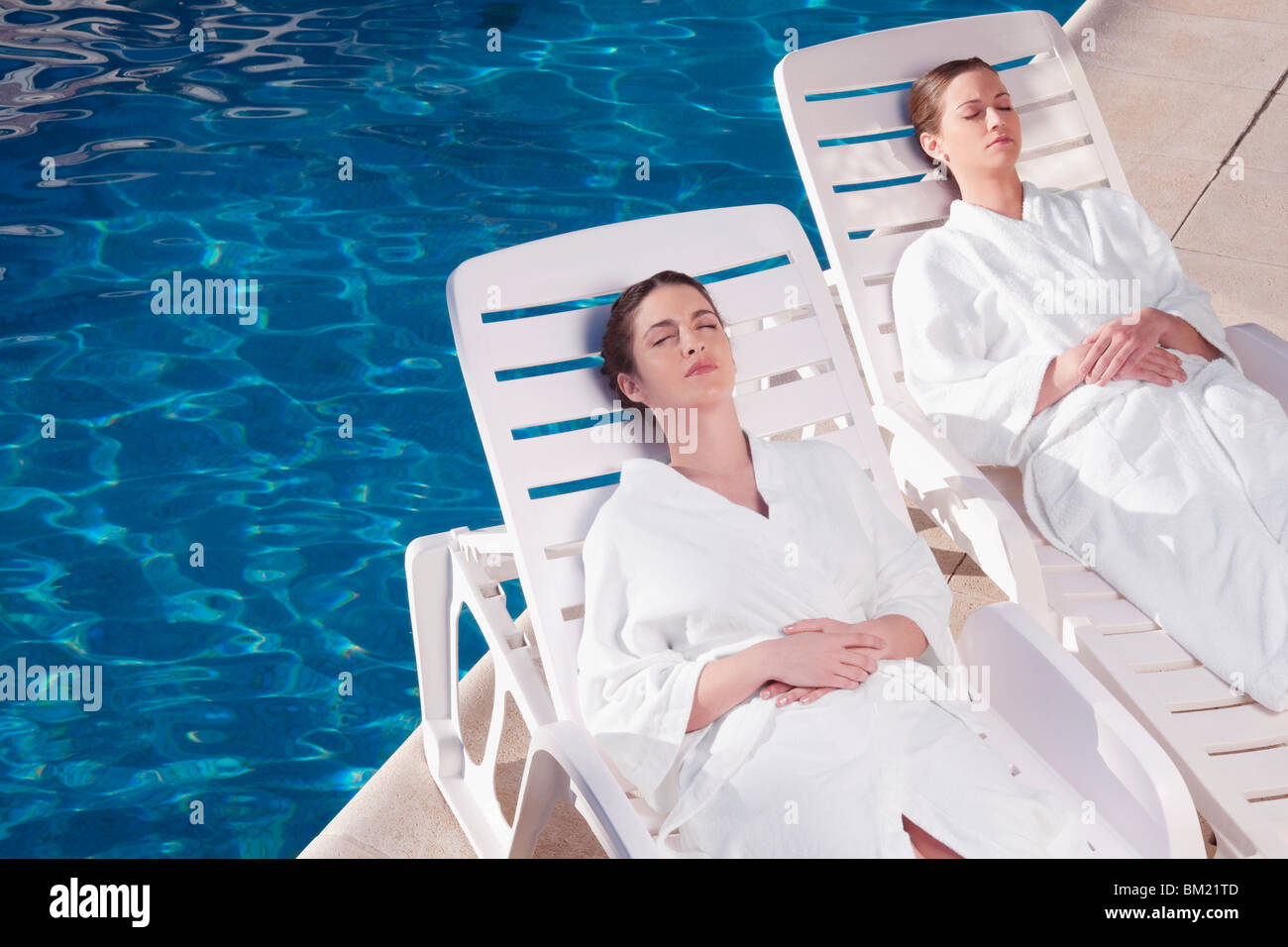 Two women resting on lounge chairs at poolside Stock Photo - Alamy