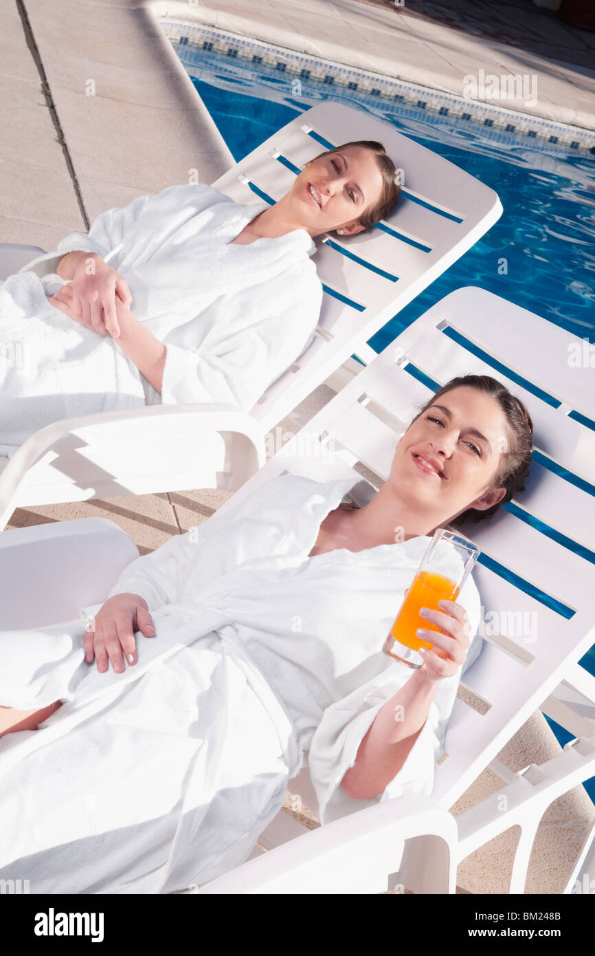 Two women resting on lounge chairs at poolside Stock Photo - Alamy