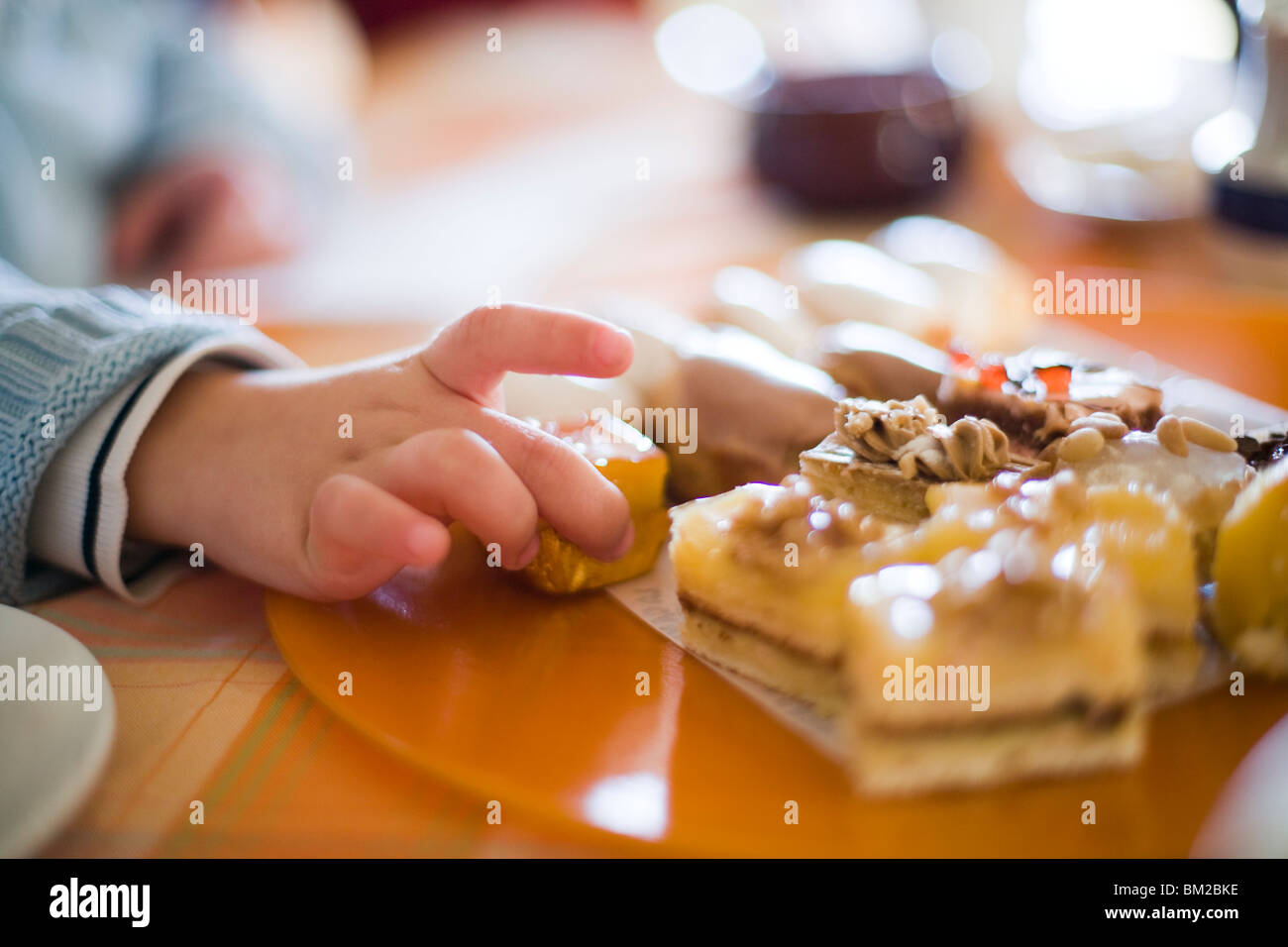 Child's hand picking up a sweet from a plate with assorted sweets ...