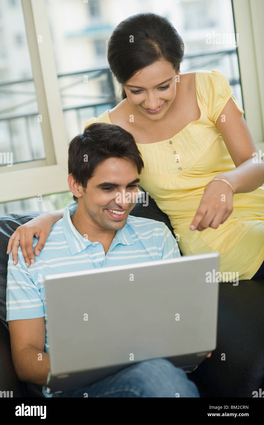 Couple sitting on a couch and working on a laptop Stock Photo - Alamy
