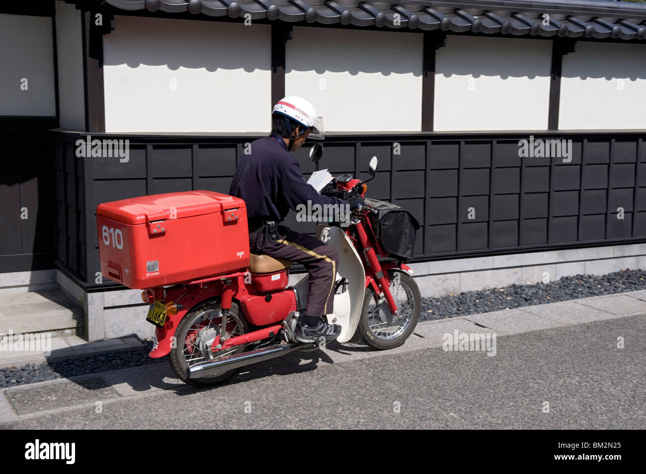 A Japanese postman riding a typical red scooter making his rounds ...