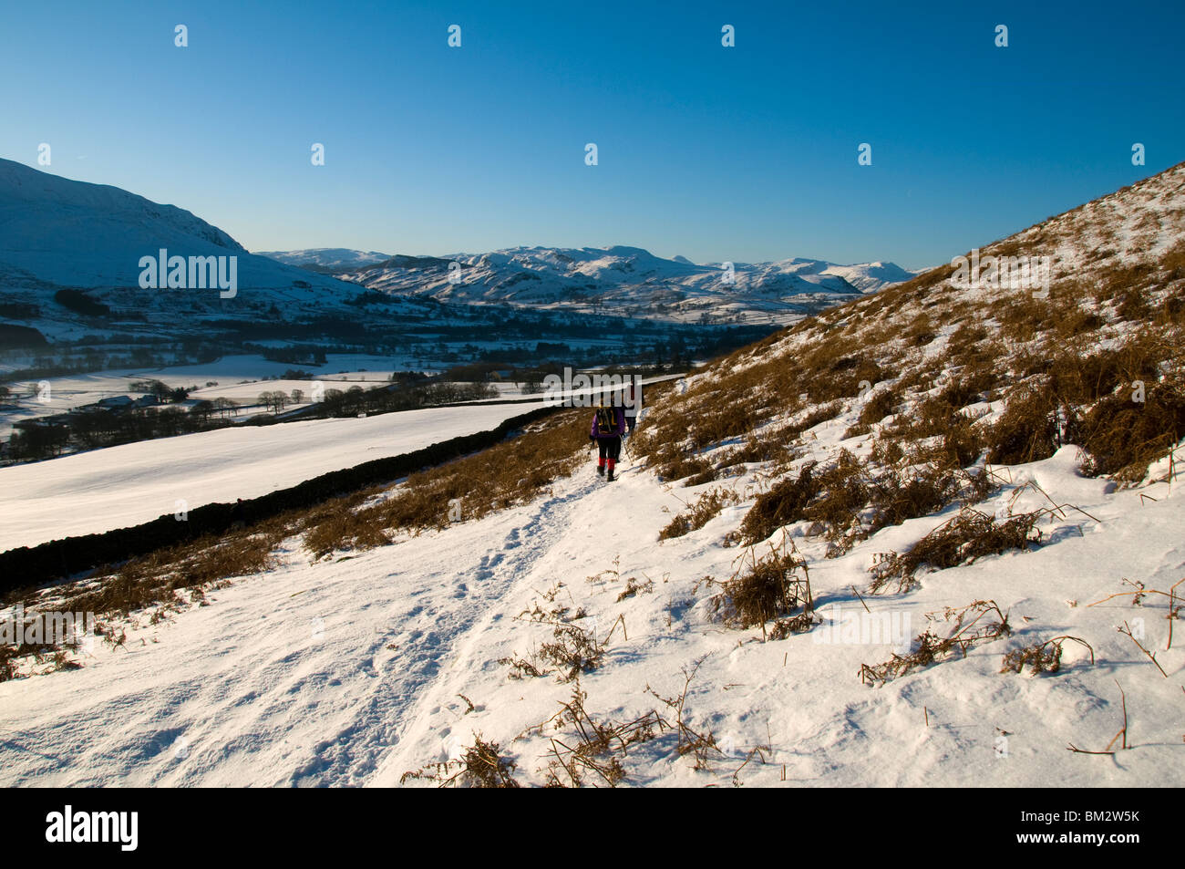 Walkers on a path on the lower slopes of Blencathra in winter. Lake ...