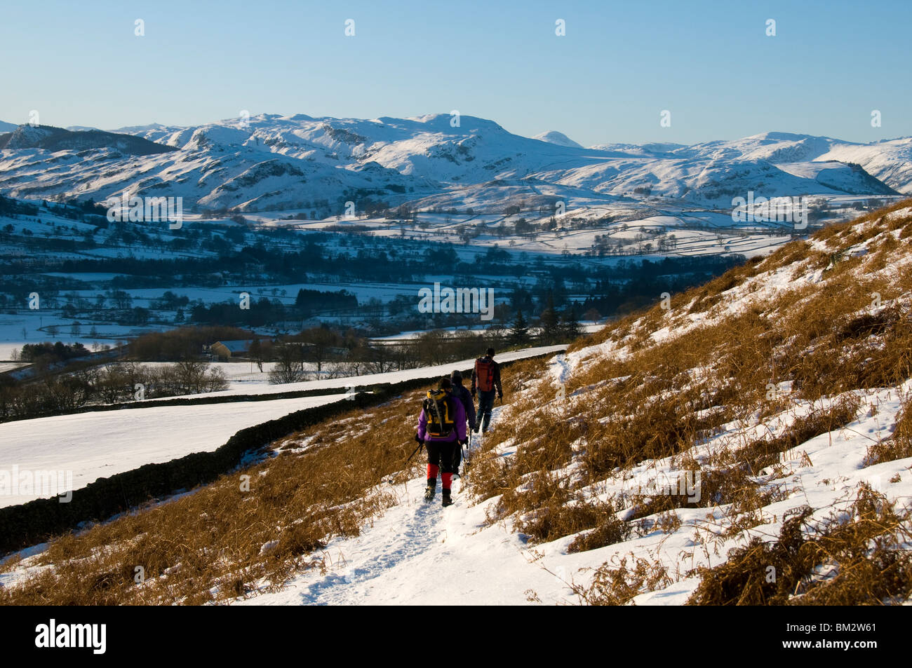 Walkers on a path on the lower slopes of Blencathra in winter. Lake ...