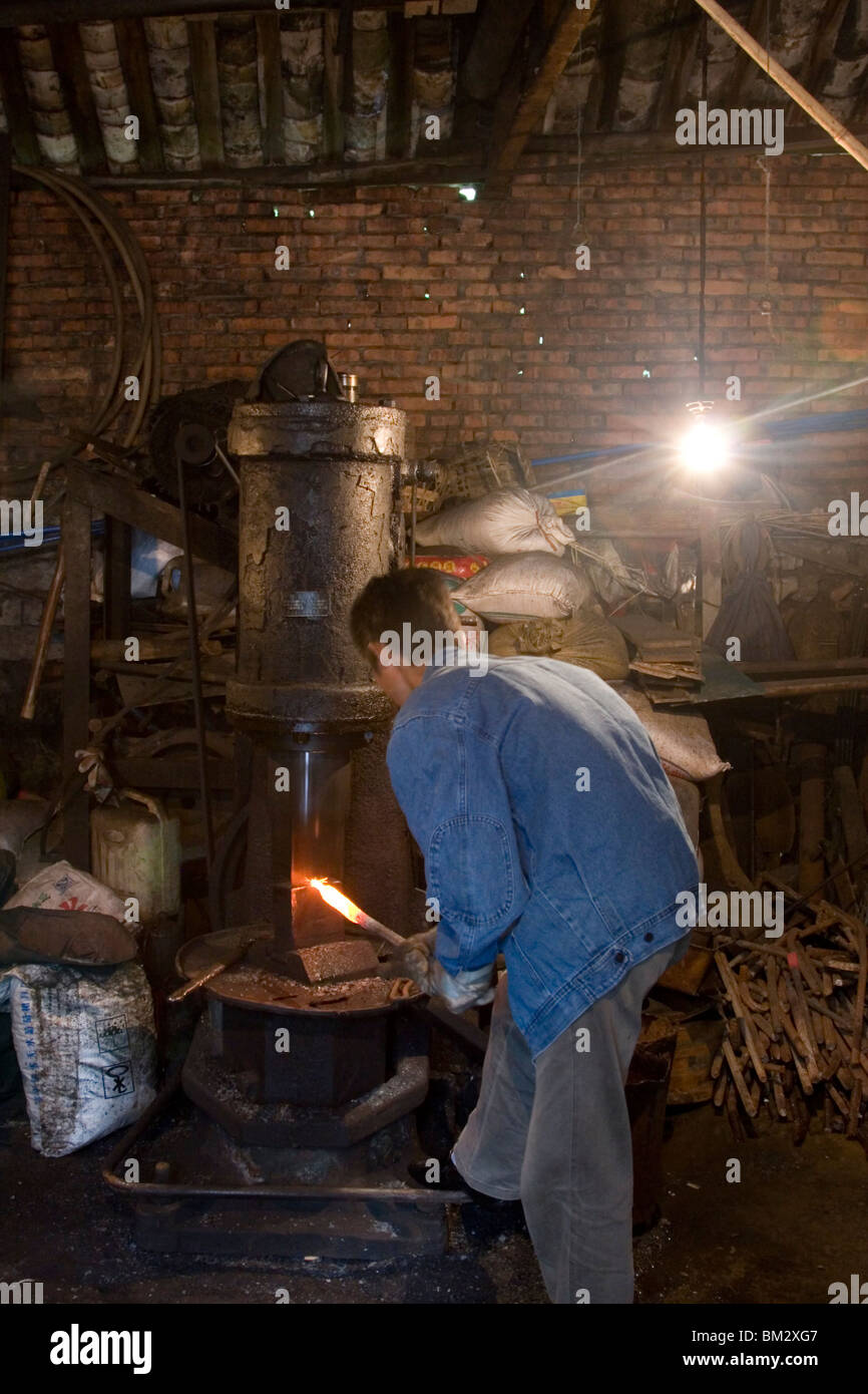 A blacksmith working on a die forge in his workshop in Sichuan in China ...