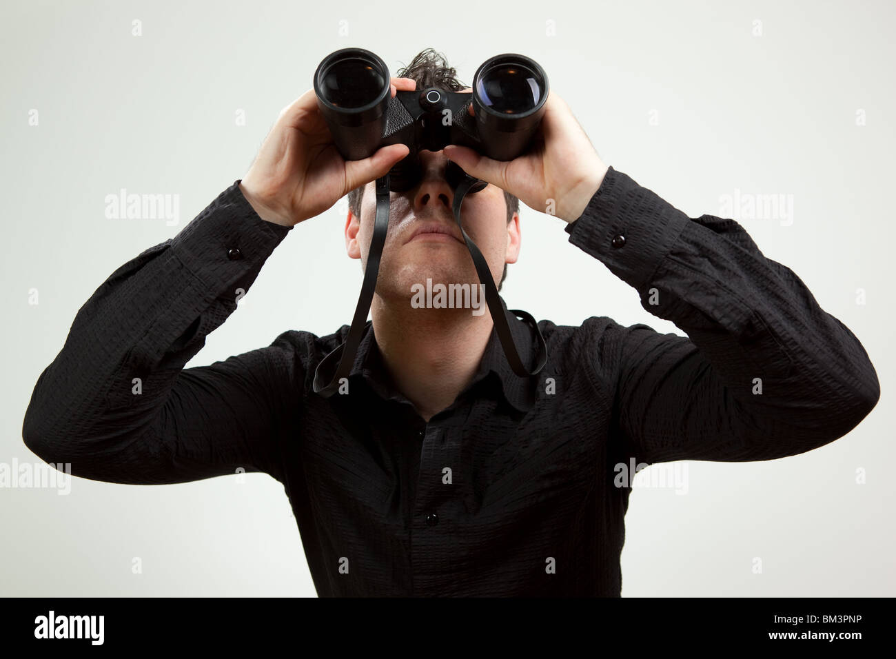 Young man wearing black shirt and holding binoculars, isolated on white ...