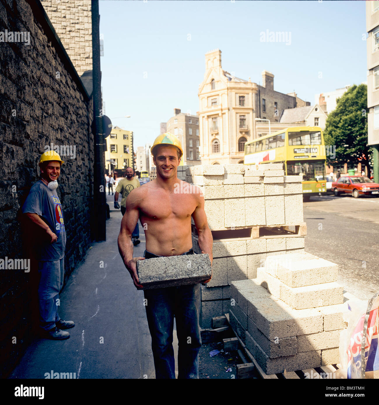 Smiling shirtless construction worker lifting a half cement breeze ...