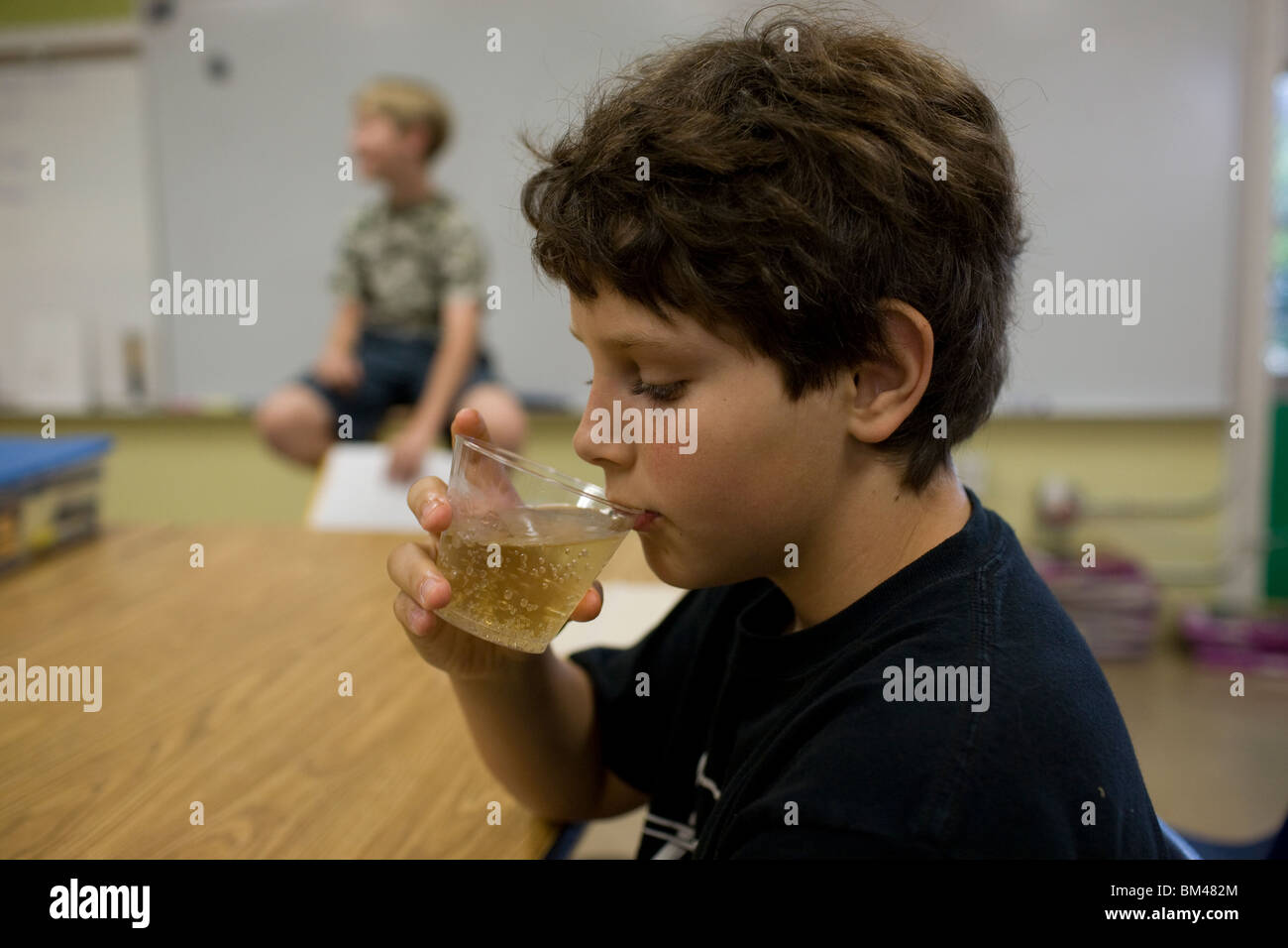 11-year-old Anglo boy sips ginger ale from a plastic cup at a school ...