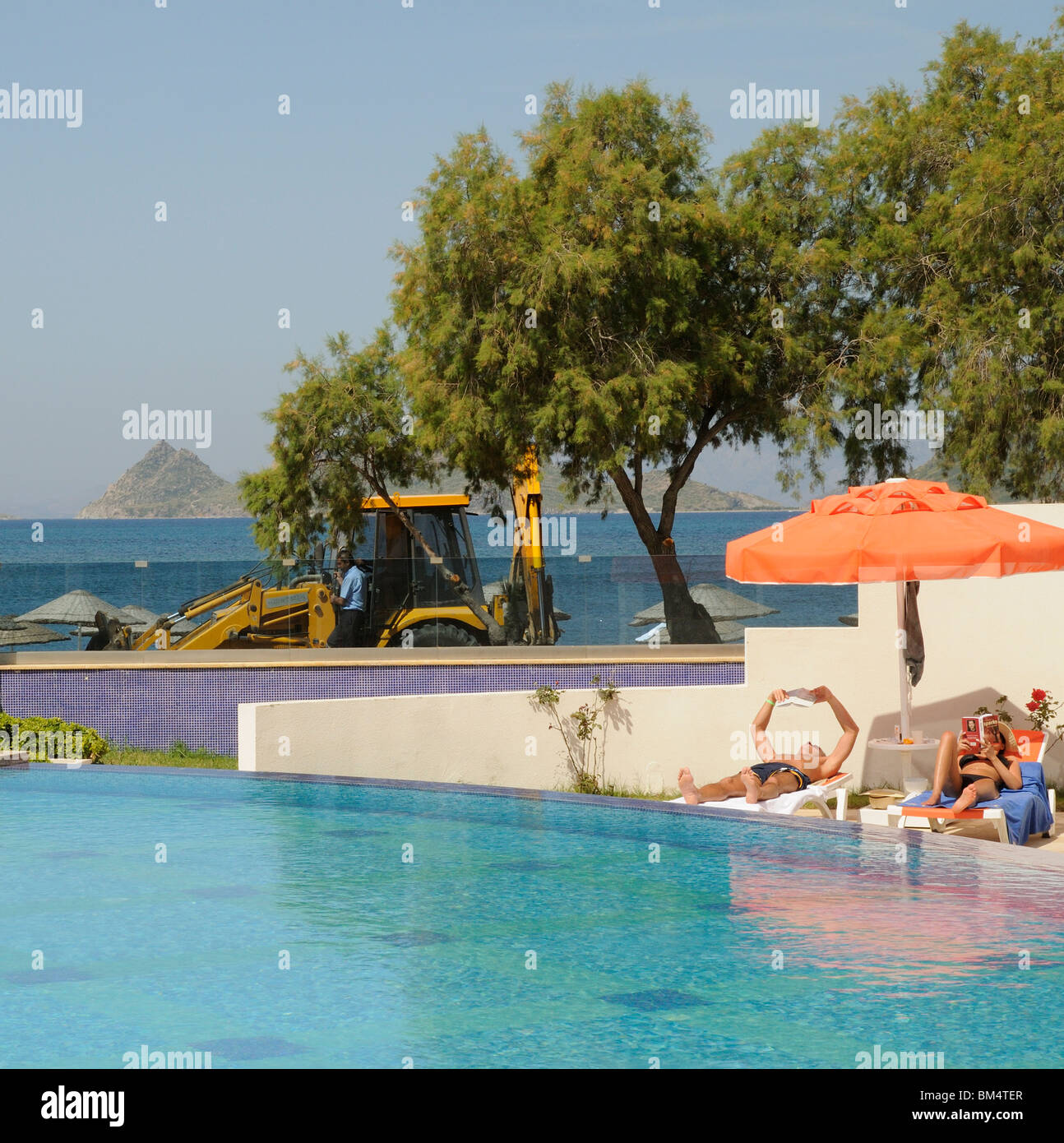 Holidaymakers try to relax by the pool with a mechanical digger working ...
