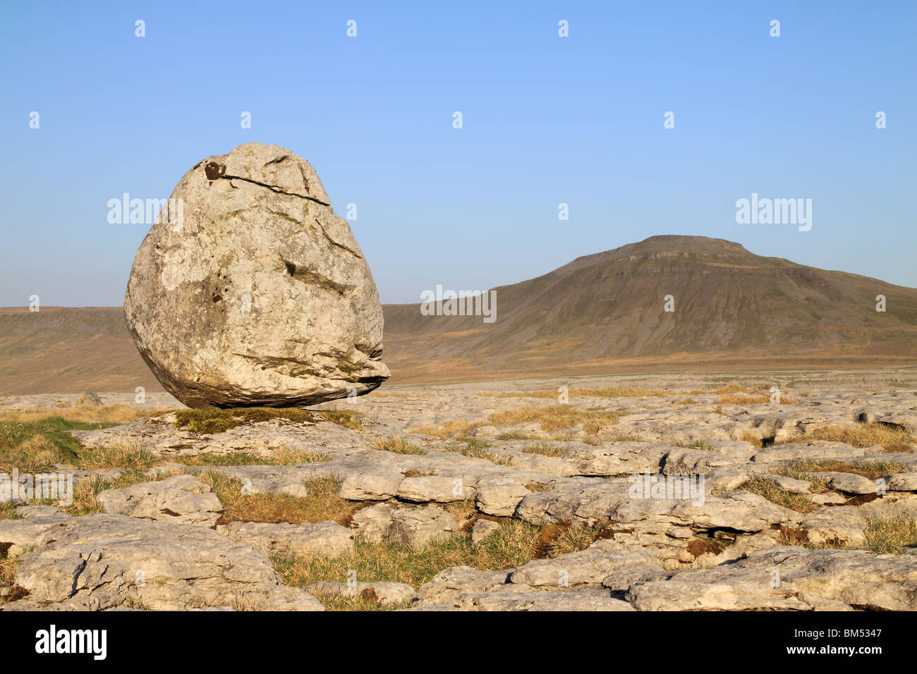A boulder stands on limestone pavement with Ingleborough in the ...