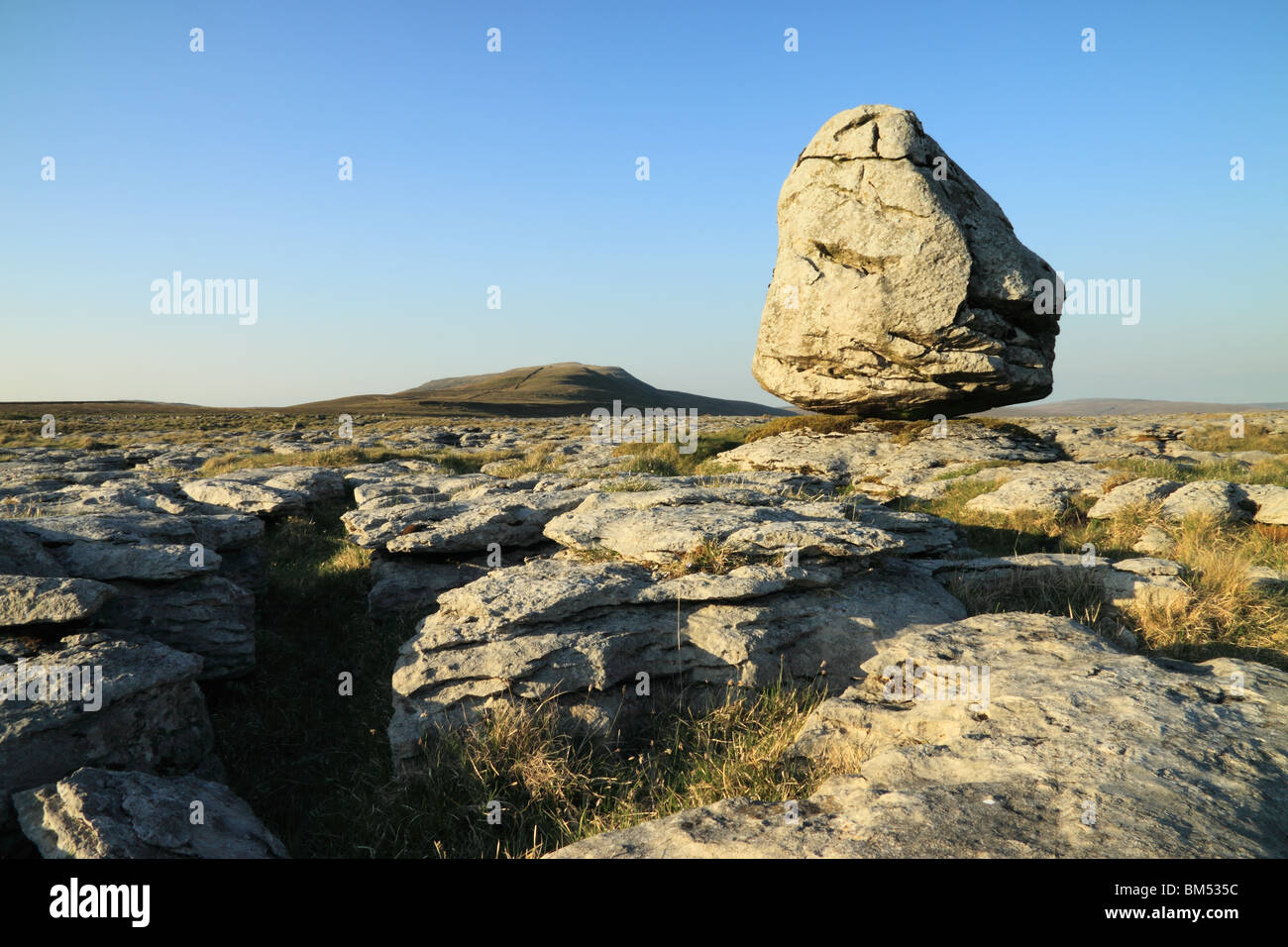 A boulder stands on limestone pavement with Whernside in the distance ...