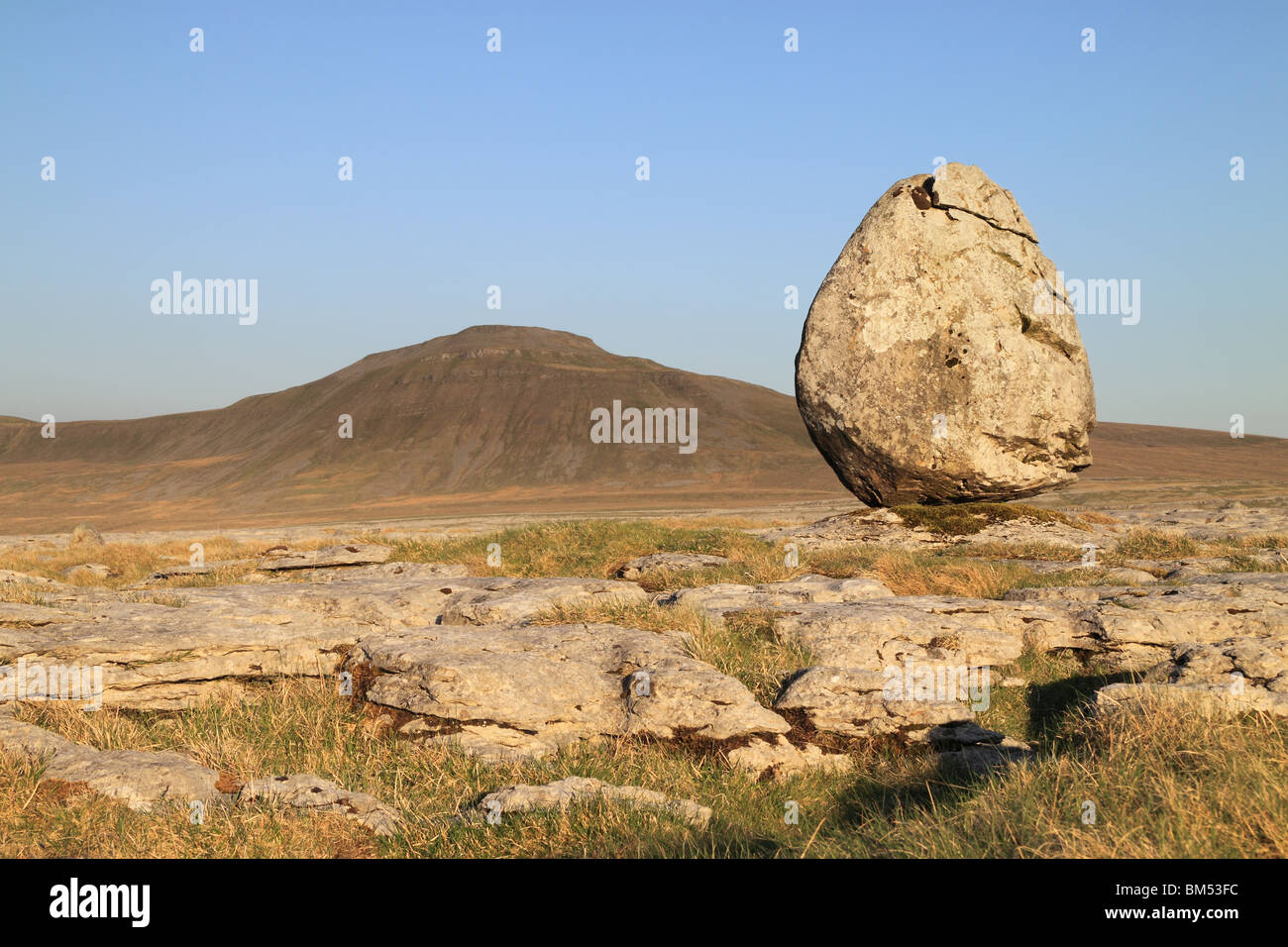 A boulder stands on limestone pavement with Ingleborough in the ...