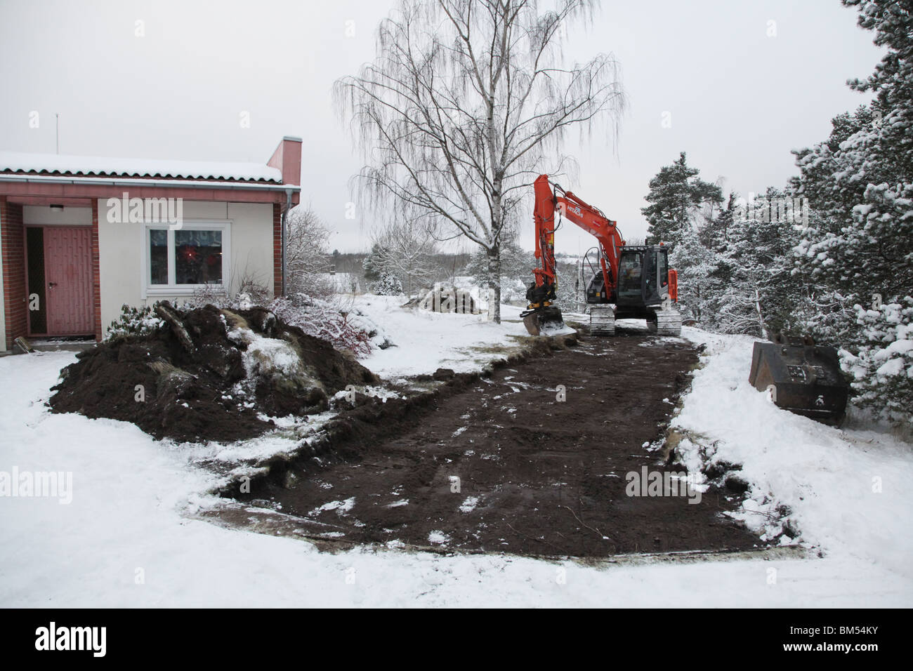 A digger excavator clears a path through snow to make a work road next ...