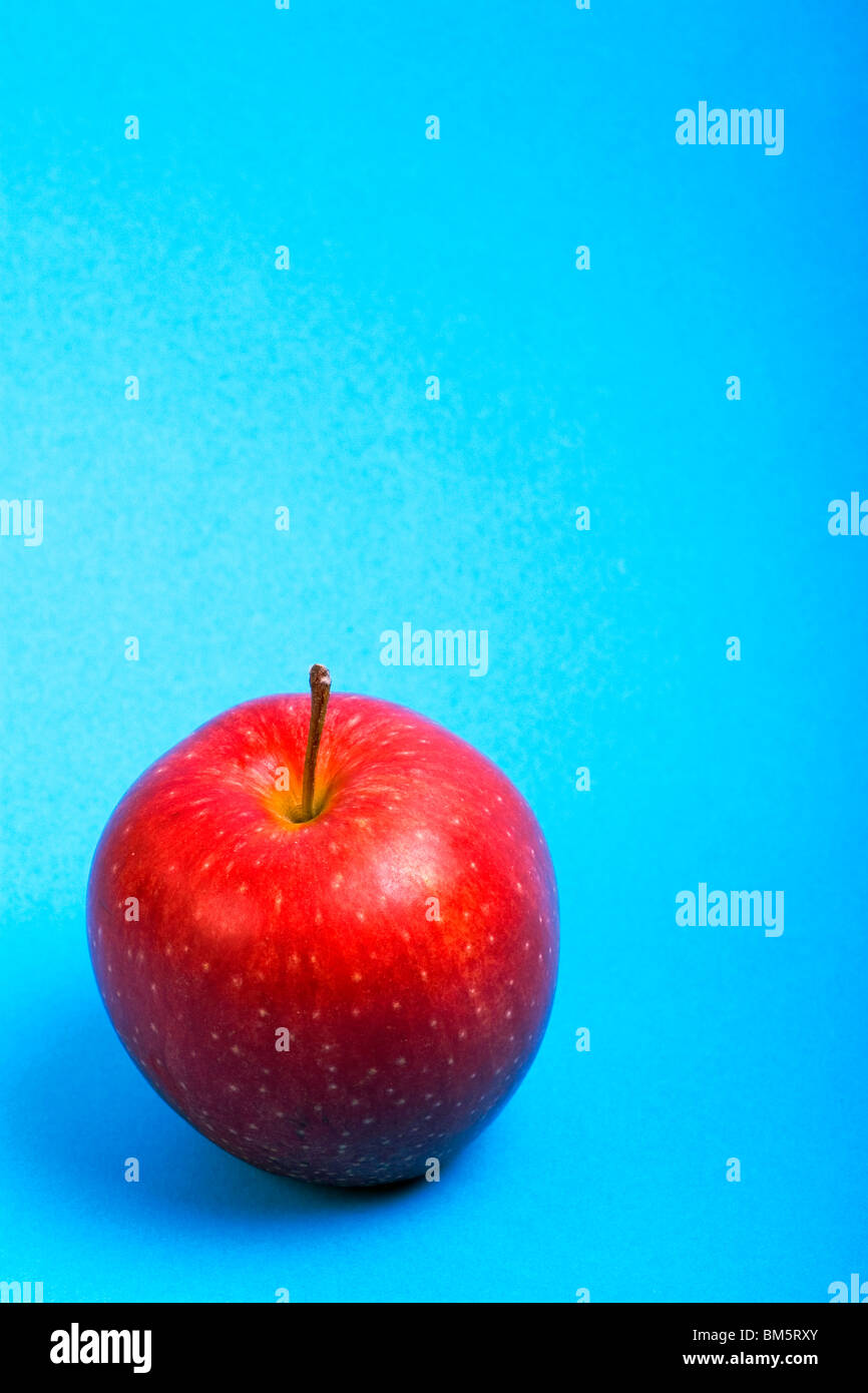 a shiny red apple with stalk sits on an aqua blue background with ...