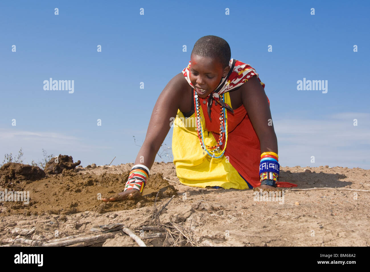 Masai woman repairing the roof of a hut with cow dug, Masai Mara, Kenya ...