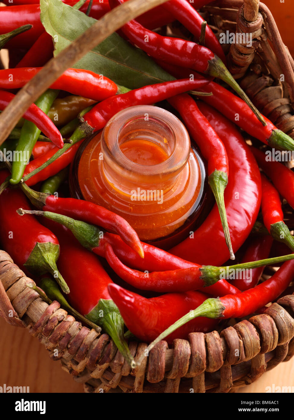 A glass bottle of chilli sauce in a basket with red chillies Stock ...