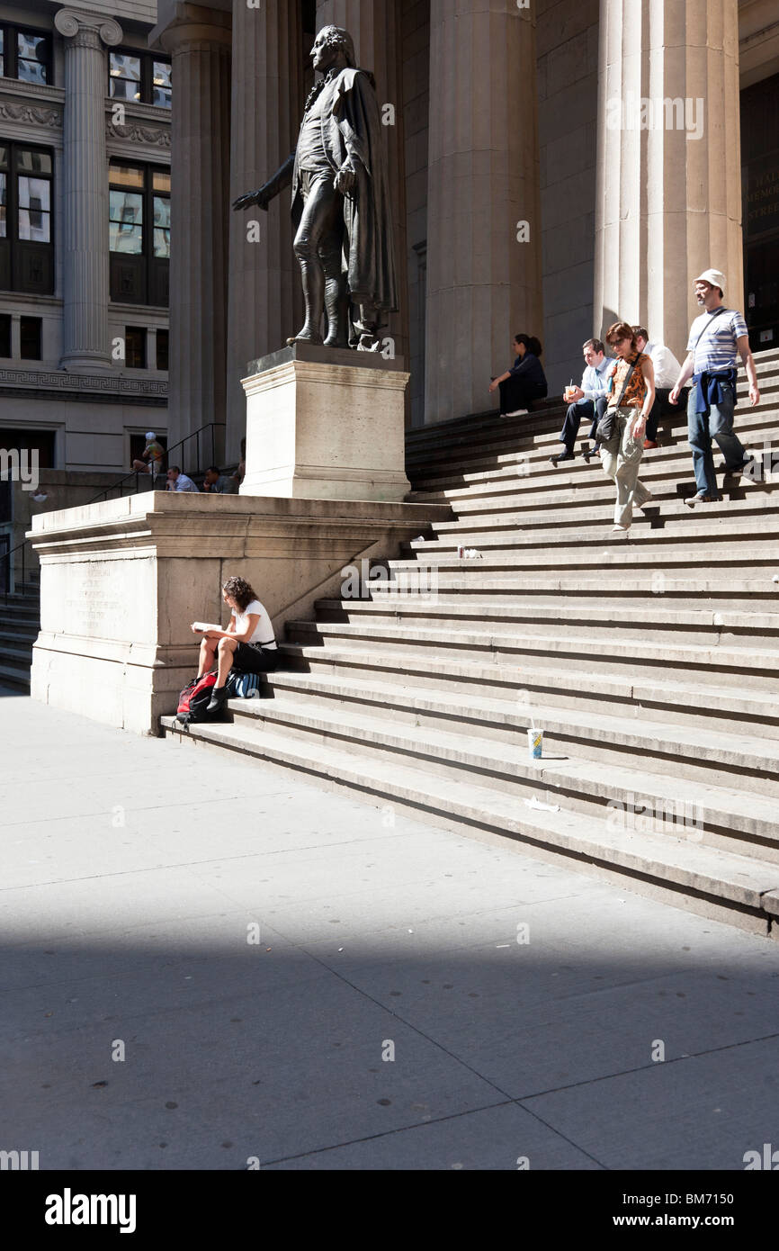 young woman reading in sun on steps of Federal Hall next to bronze ...