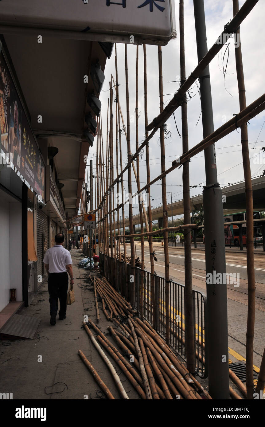 Man walking on a pavement in front of shops with bamboo scaffolding ...