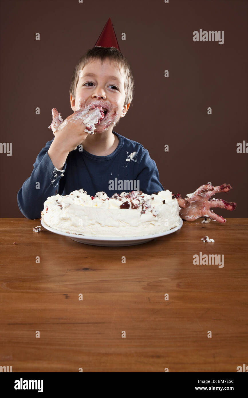 A boy wearing a party hat eating pie with his hands, studio shot Stock ...
