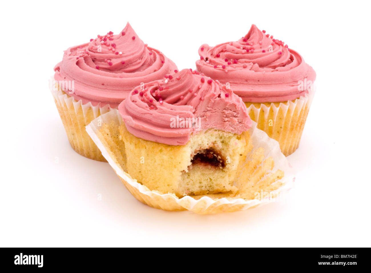 three pink cup cakes on a white background with one bite taken Stock ...