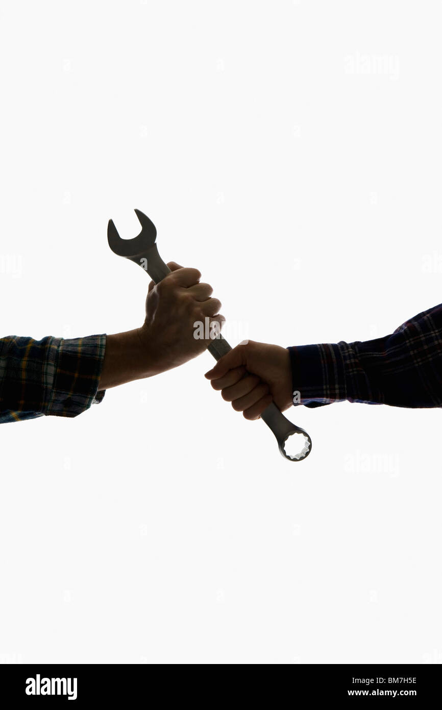 A construction worker handing a wrench to another worker, focus on ...