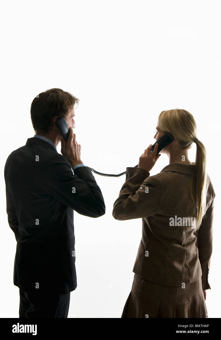 Two business people using phone receivers connected with the same cord ...