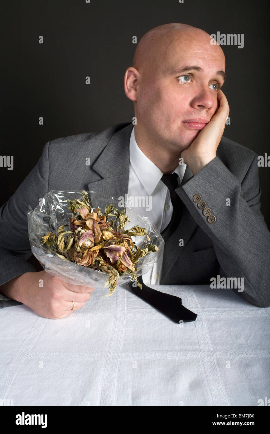 A well-dressed man holding a bouquet of dead flowers and looking sad ...