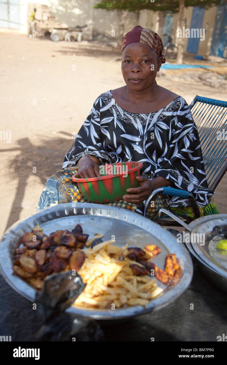 A woman sells fried plantains (alloco) and potatoes for breakfast next ...