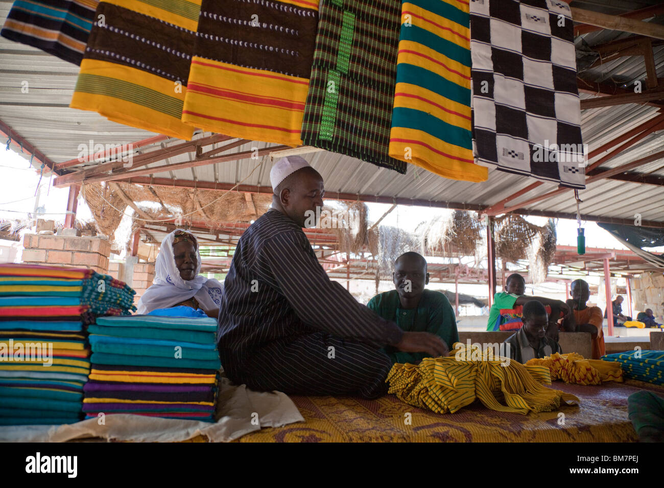 A Fulani man sells strips of cloth woven together into colorfully ...