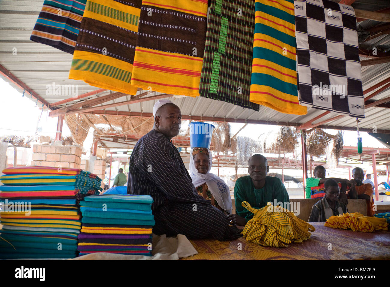 A Fulani man sells strips of cloth woven together into colorfully ...