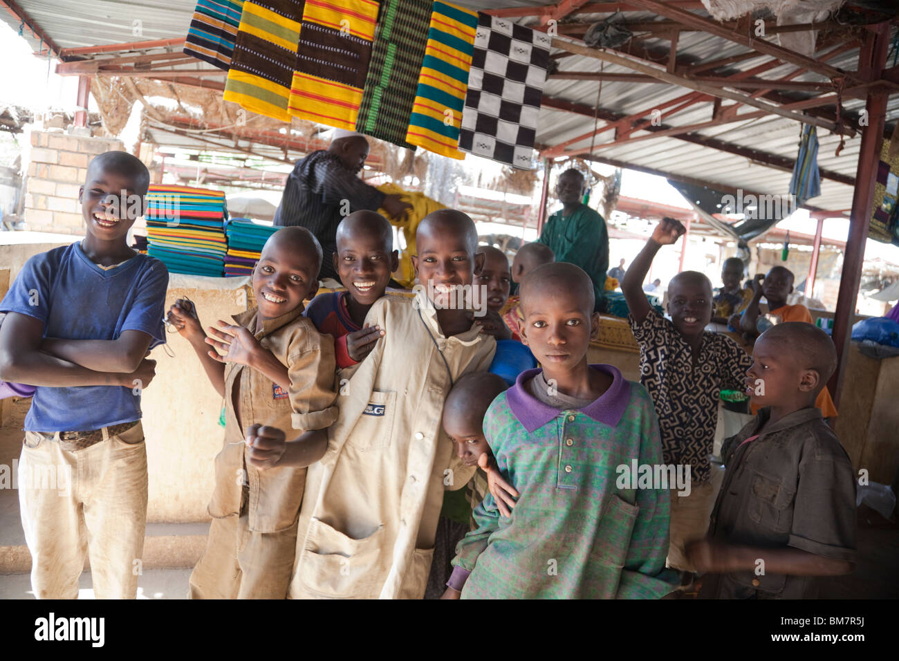 Fulani children pose in front of a market stall selling colorful woven ...