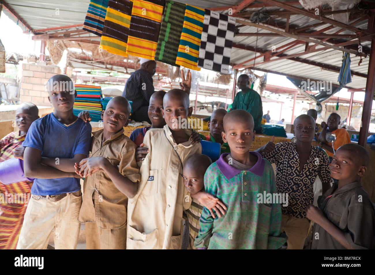 Fulani children pose in front of a market stall selling colorful woven ...