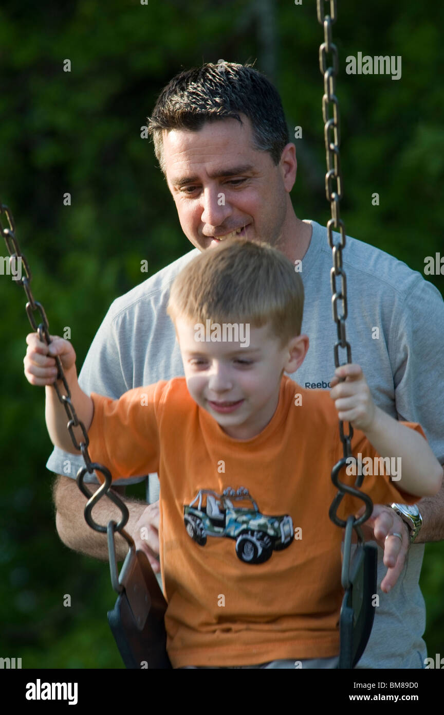 Italian father in his forties pushes his four year old son on a swing ...