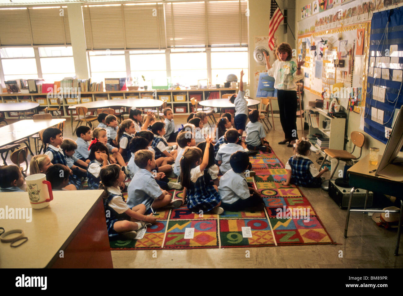 Teacher explains lesson to class as students sit on floor in front of ...