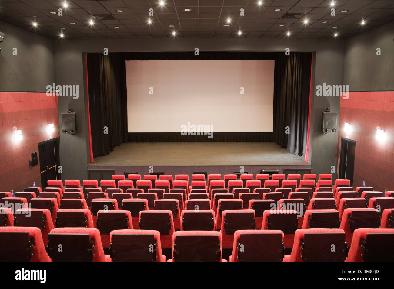 Empty cinema auditorium with line of red chairs, stage and projection ...