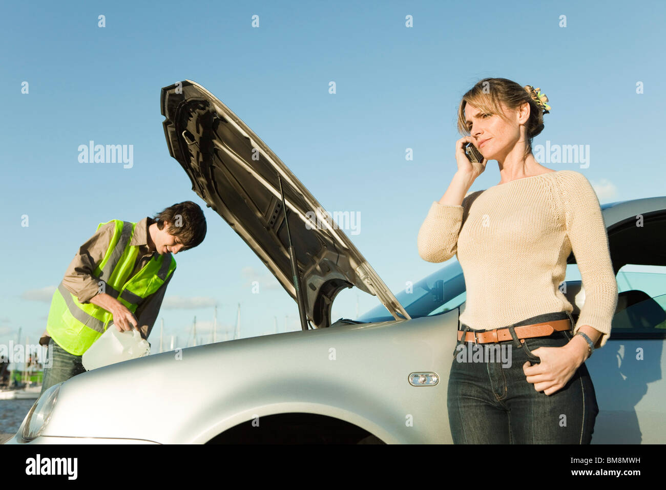 Woman making phone call while roadside assistance mechanic works to ...