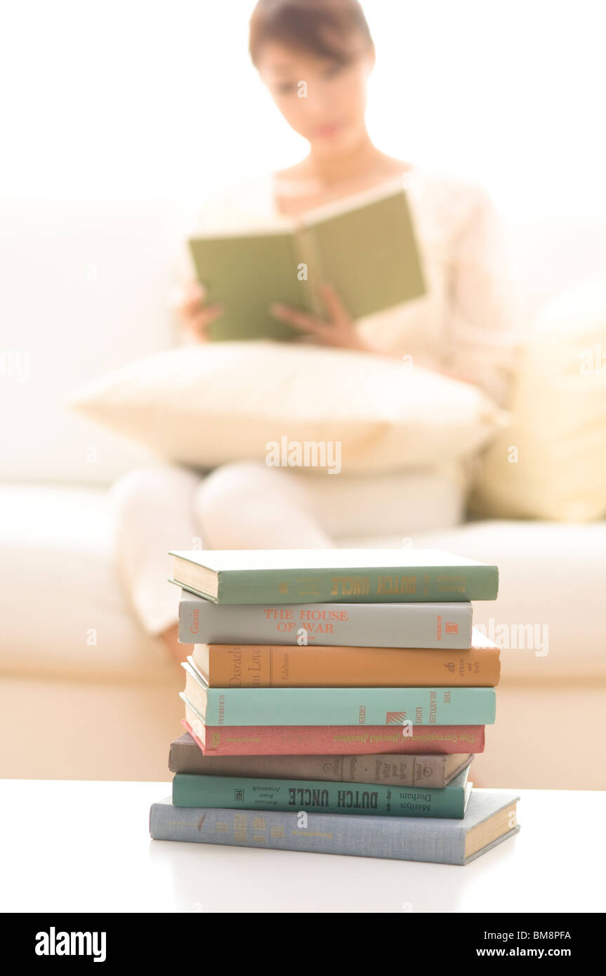 Stack of books with woman reading a book in background Stock Photo - Alamy