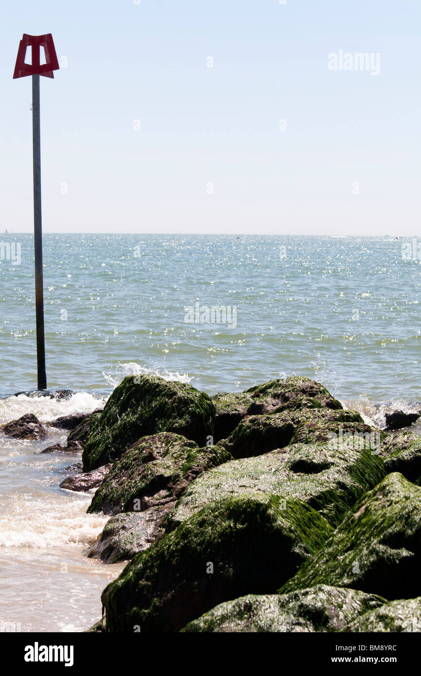 seaweed covered stone groyne wih red marker pole on Muneford beach ...