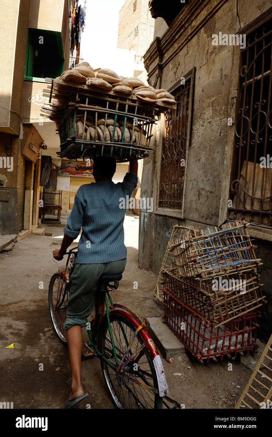 Man carrying bread on his head while riding a bicycle in islamic Cairo ...